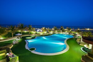 Uma piscina grande e curvilínea com um deck ao redor, palmeiras e espreguiçadeiras.
