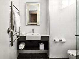 Um banheiro moderno com pia branca, espelho, porta-toalhas, vaso sanitário e prateleira com caixa de lenços.