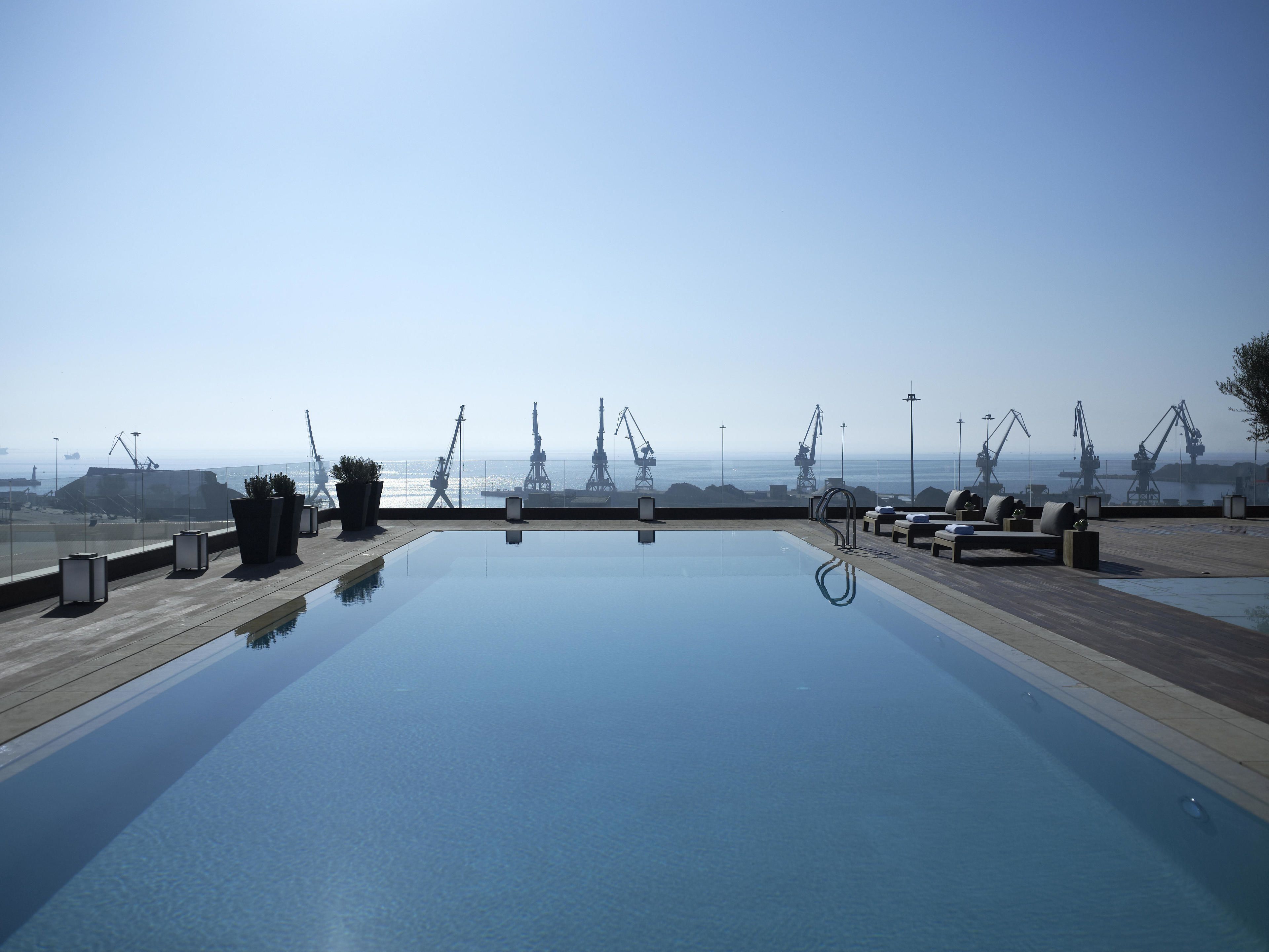 Piscina infinita no terraço com vista para o oceano e guindastes industriais.