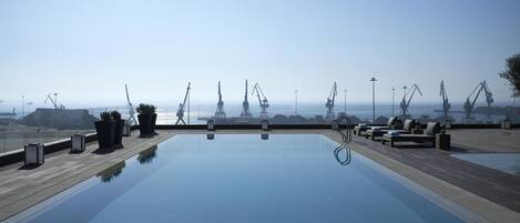 Piscina infinita no terraço com vista para o oceano e guindastes industriais.