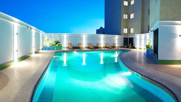 Uma piscina com espreguiçadeiras e um deck revestido de azulejos, cercada por um edifício com fachada em azulejo azul.