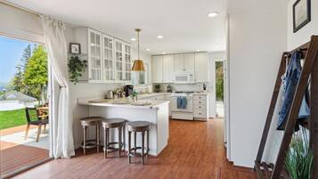 Uma cozinha moderna com armários brancos, uma ilha central com banquetas, micro-ondas e vista para o exterior.