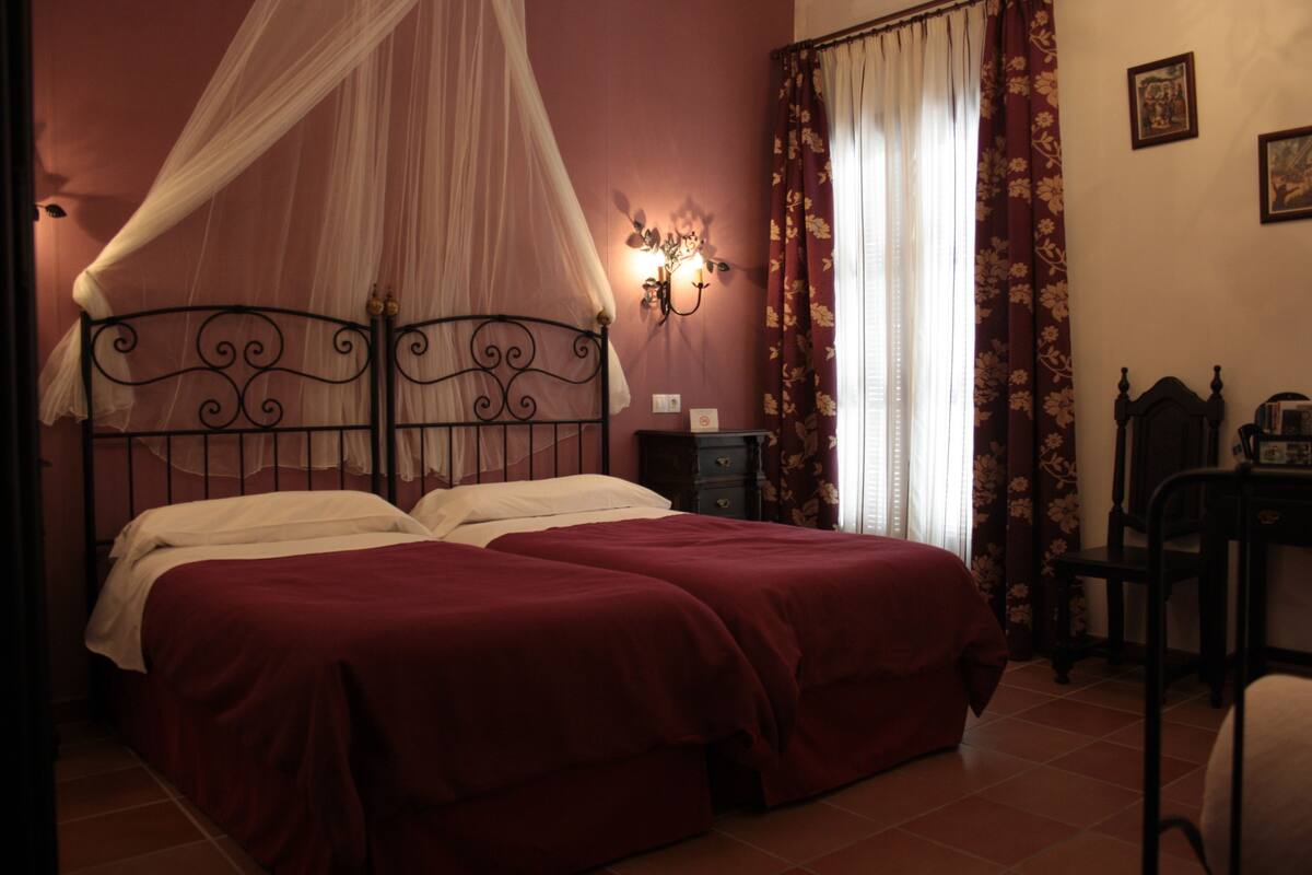 Quarto com cama de dossel, mesa de cabeceira e cadeira.
