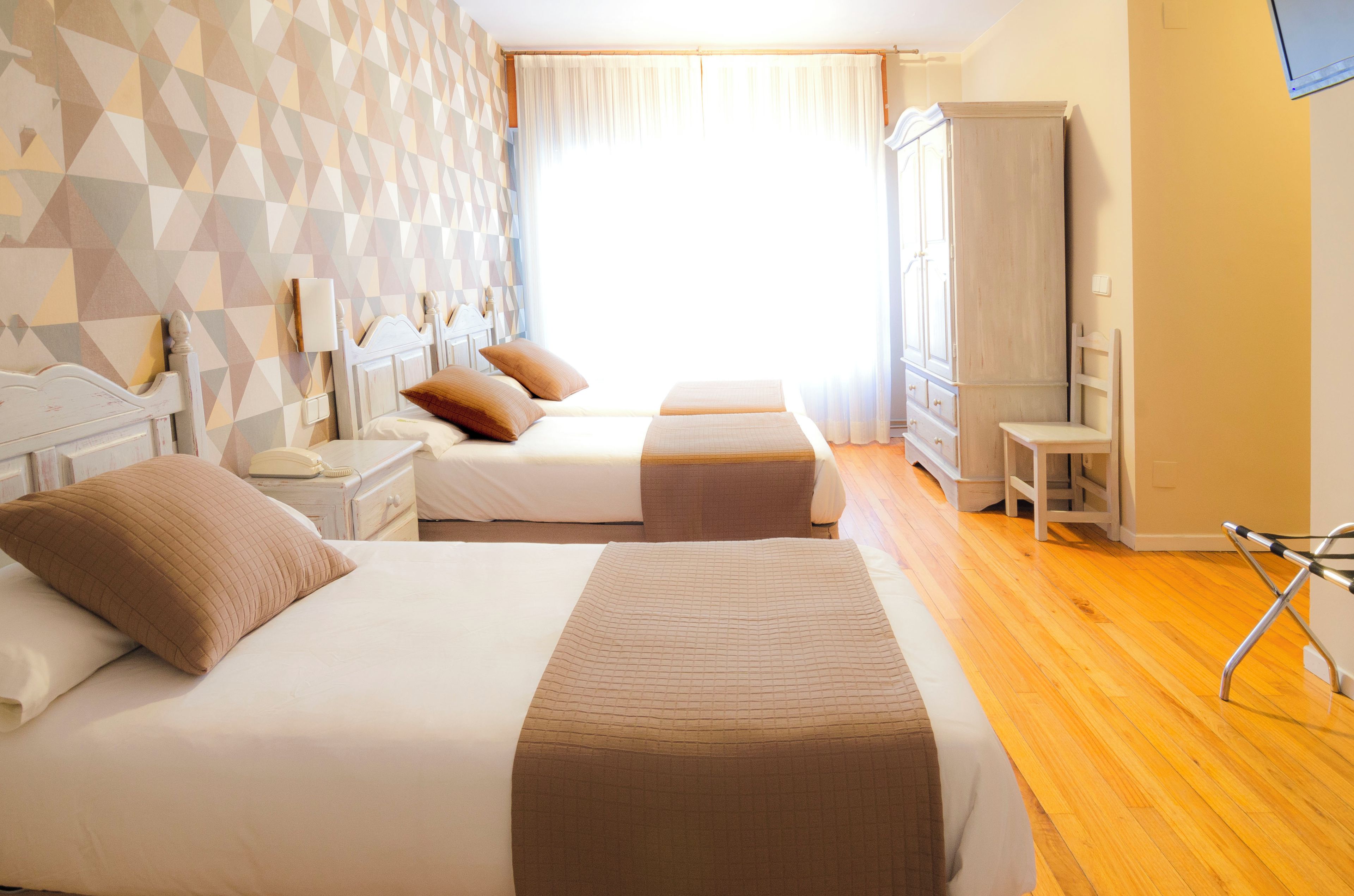Quarto de hotel com duas camas, um guarda-roupa, uma escrivaninha e uma cadeira.