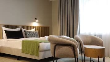 Quarto de hotel com cama, duas cadeiras, uma mesa redonda e um abajur.