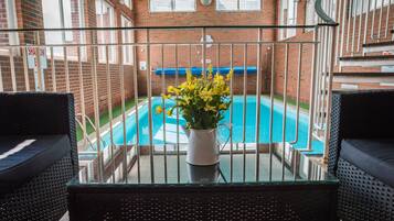 Uma varanda com mesa de vidro, planta em vaso e vista para uma piscina.