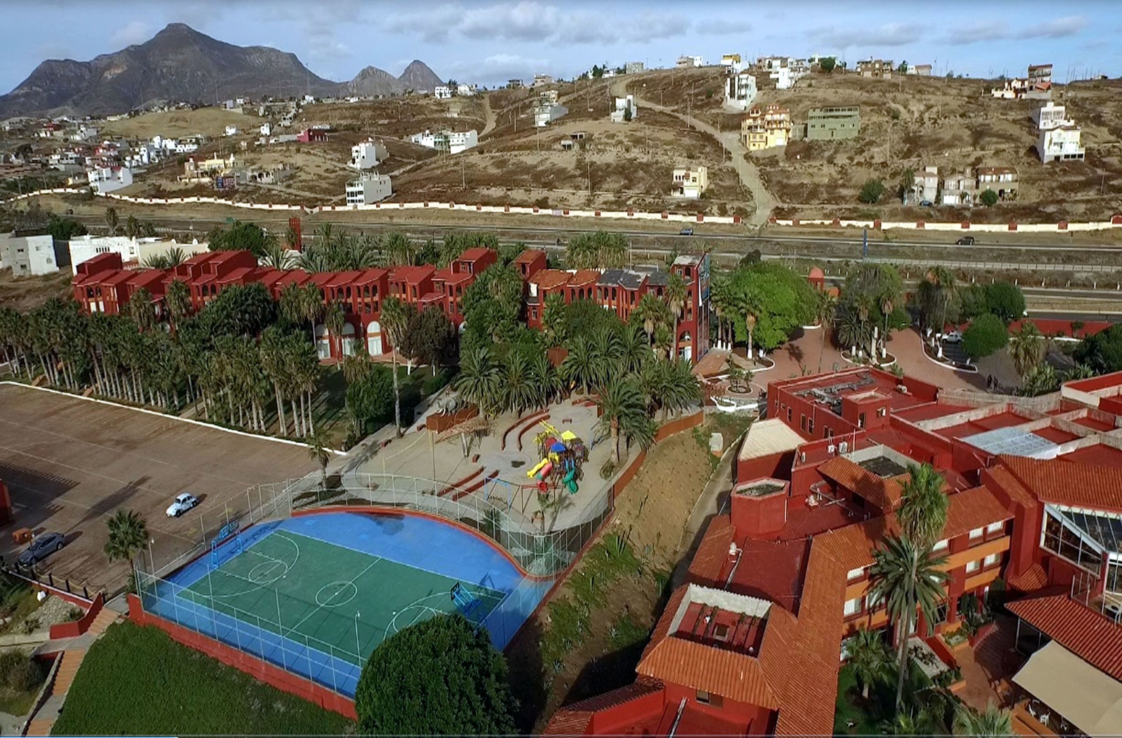 Um bairro residencial com edifícios de telhado vermelho, quadra de basquete e parquinho.