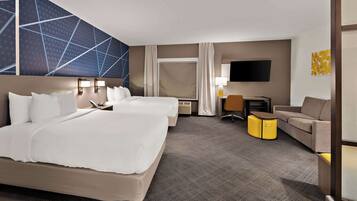 Quarto de hotel com uma cama grande, um sofá, uma escrivaninha com cadeira, televisão de tela plana e um painel decorativo.