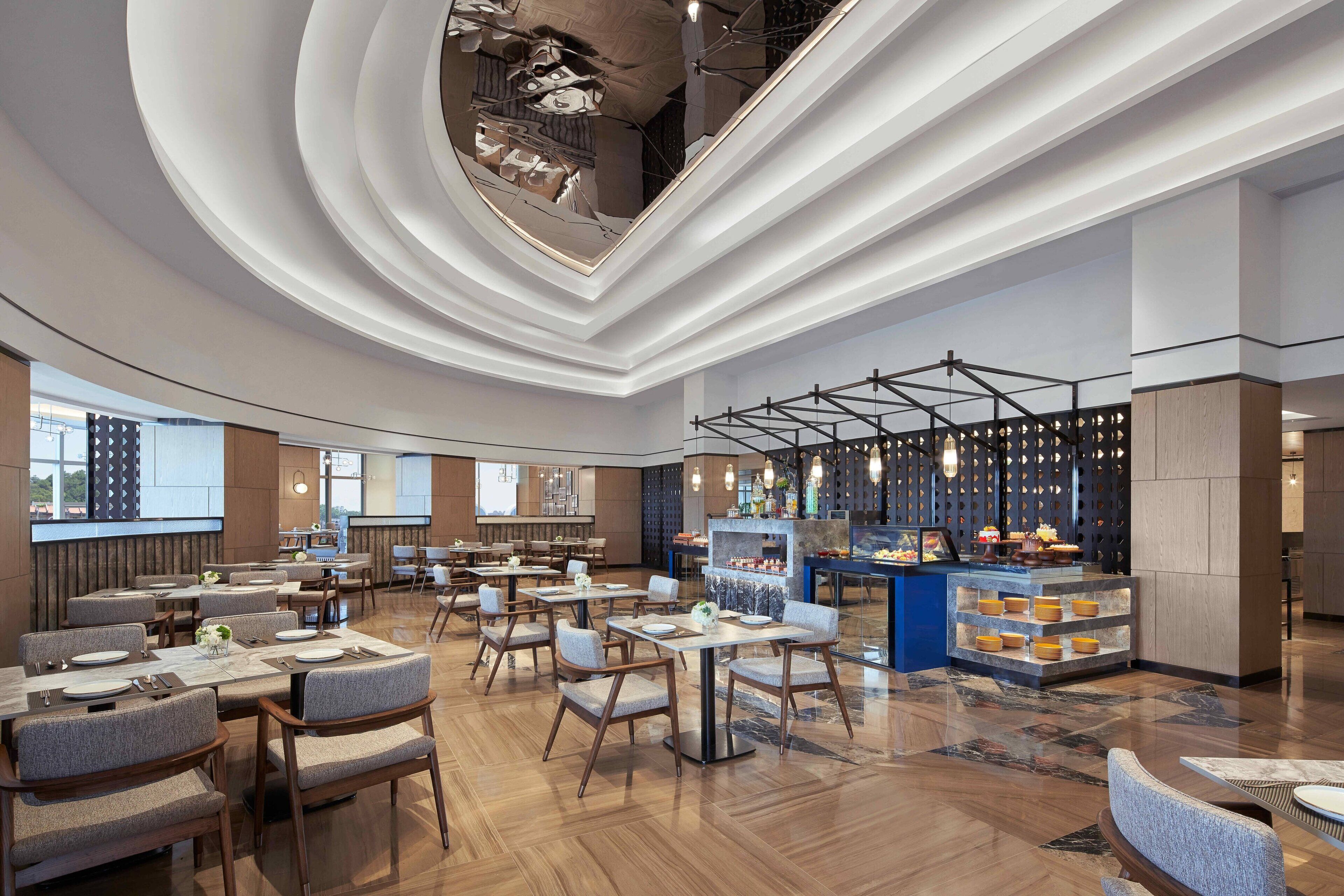 Um amplo hall de hotel com várias áreas de refeições, um bar central e um design de teto moderno.
