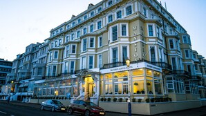 Um edifício em esquina com vários andares, com um hotel em destaque chamado "Mansion (Lions) Hotel", com estilo arquitetônico clássico.