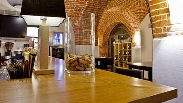 Interior de restaurante com balcão de madeira, um pote de vidro cheio de rolhas de vinho e arcos de tijolos.