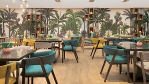 Uma sala de jantar moderna com várias mesas e cadeiras, apresentando um mural tropical na parede e prateleiras com plantas.