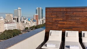 Um terraço com espreguiçadeiras, parede de madeira e vista para a cidade.