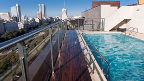 Piscina no terraço com vista para a cidade, grades de metal e um deck de madeira.
