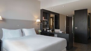 Quarto de hotel moderno com uma cama grande, abajures, escrivaninha embutida e piso de madeira escura.
