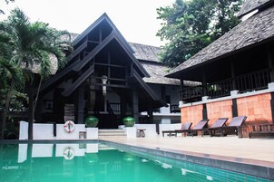 Uma área de piscina com espreguiçadeiras, um salva-vidas e um edifício com telhado inclinado.