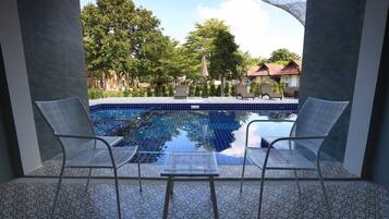 Piscina com duas cadeiras de metal e uma mesa, rodeada por azulejos estampados e vista para árvores e edifícios.