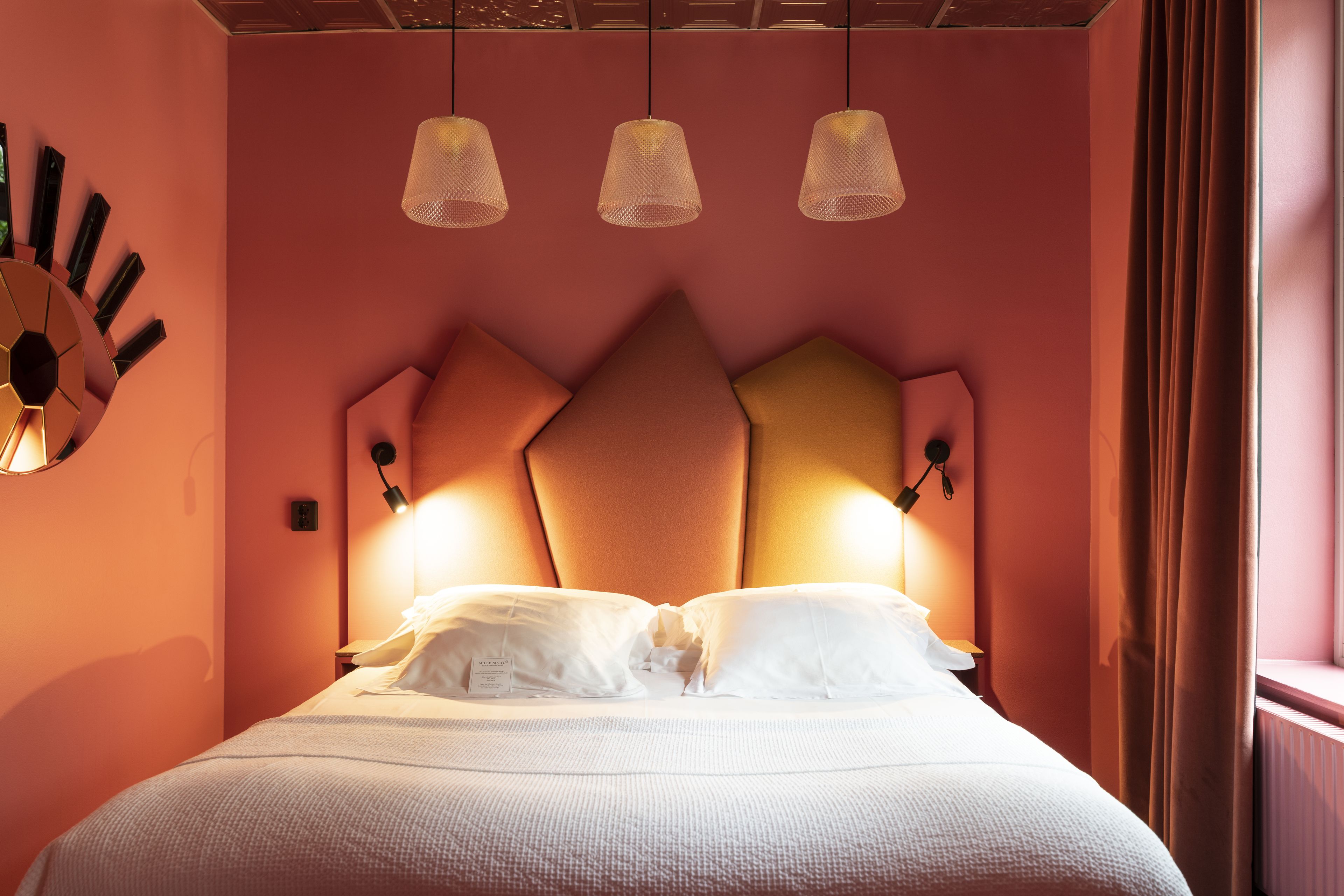 Cama bem arrumada com lençóis brancos, cabeceira moderna e três luminárias pendentes.