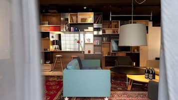 Uma sala de estar moderna com um sofá azul, uma mesa de centro e uma estante repleta de livros e objetos decorativos.