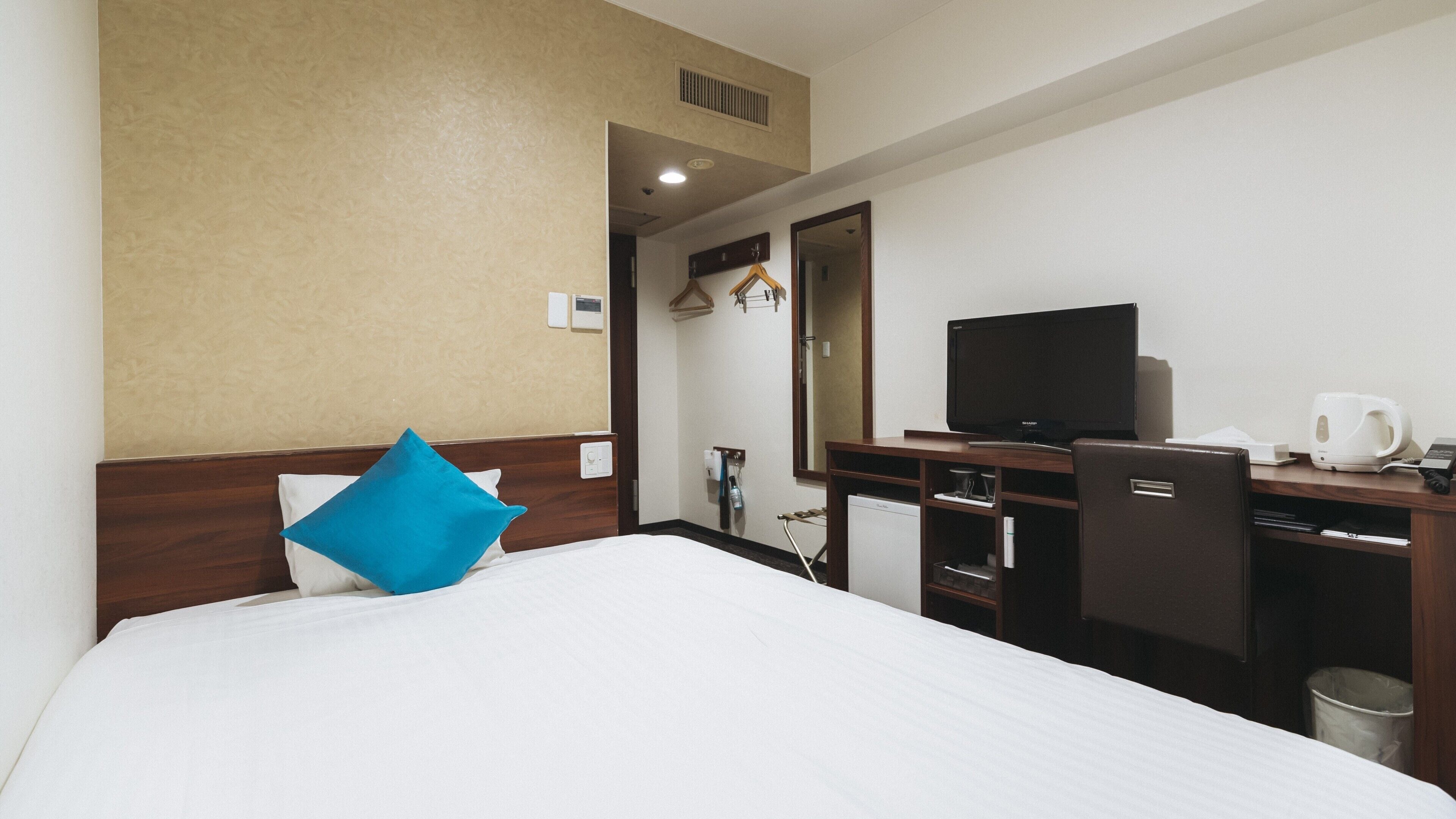 Quarto de hotel com cama, escrivaninha, televisão e cafeteira.
