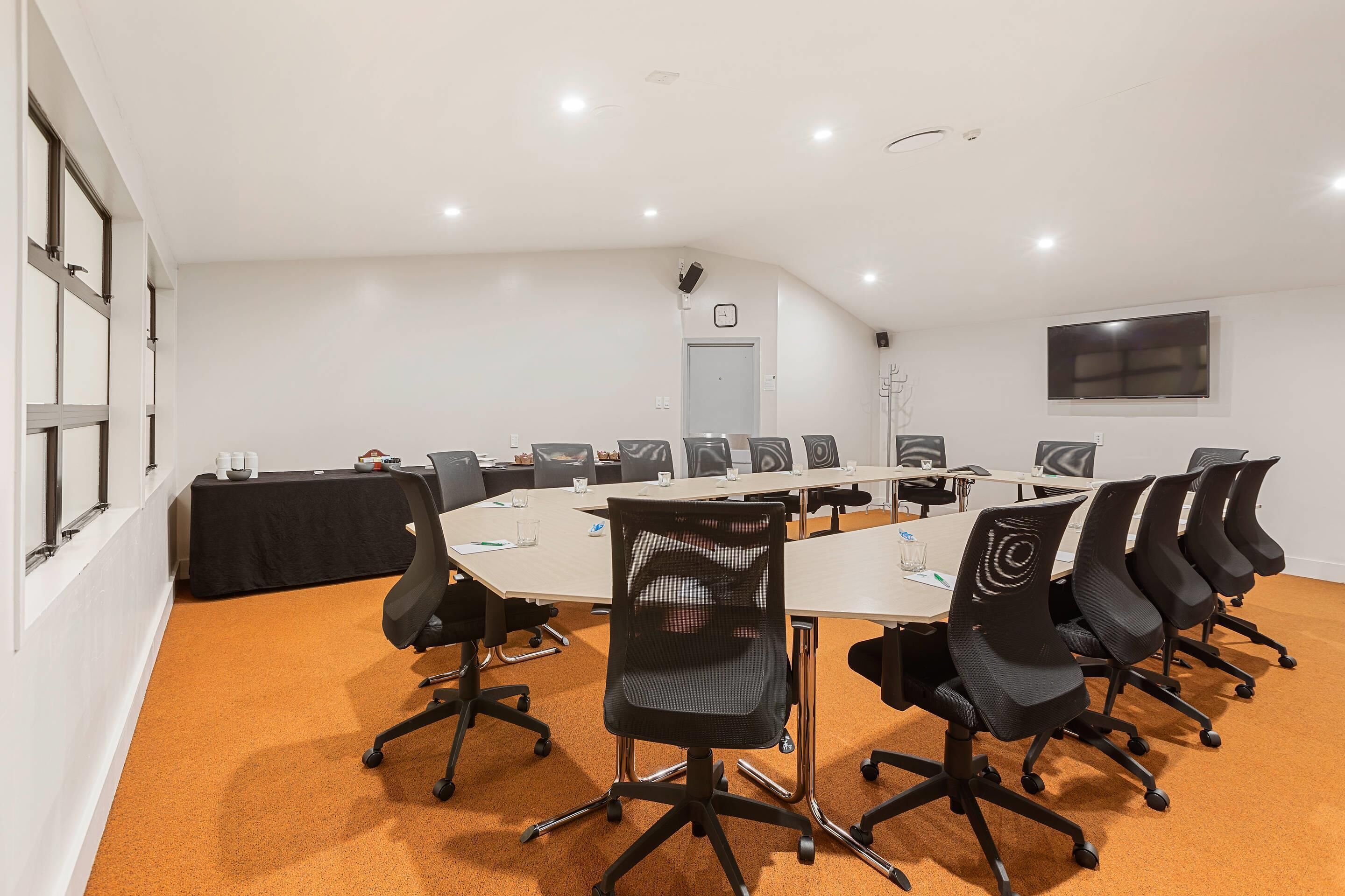 Uma sala de conferências com uma mesa comprida, cadeiras pretas e piso coberto de carpete.