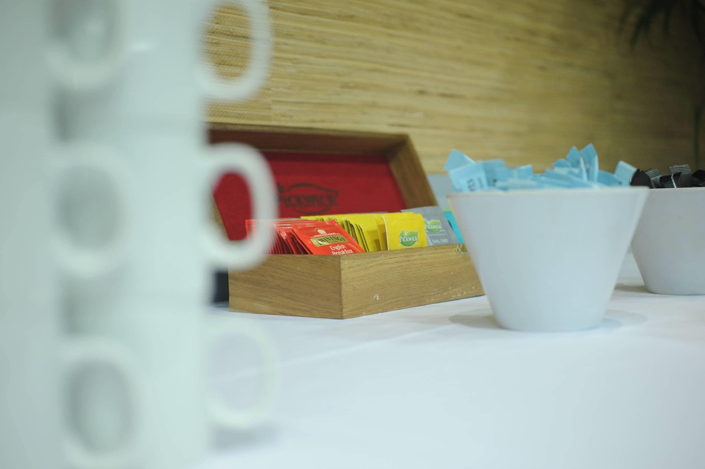 Uma caixa de madeira com lanches e uma caneca branca sobre uma mesa.