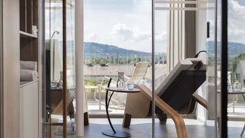 Quarto moderno com parede de vidro, mesa de madeira, uma cadeira e poltrona de massagem.