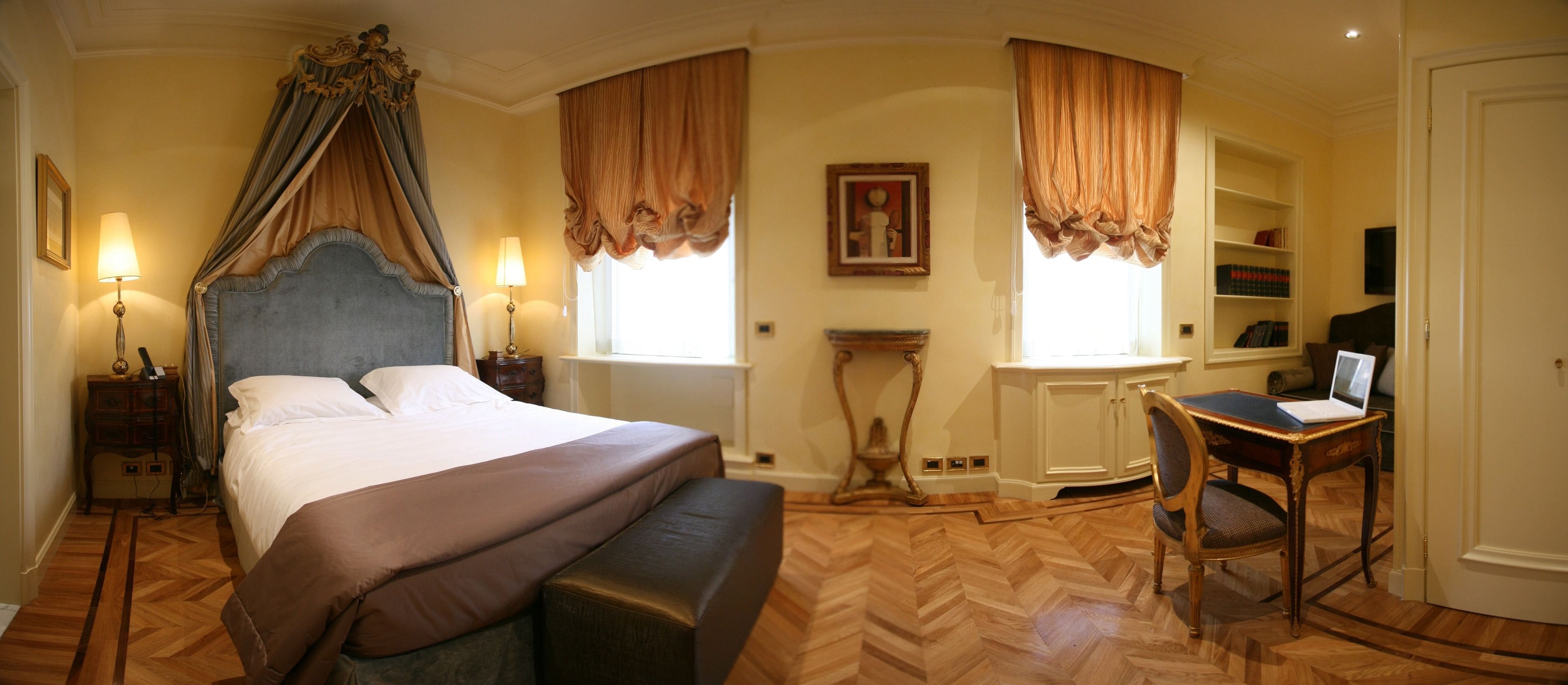 Quarto com uma cama grande, uma escrivaninha com um laptop, uma cadeira, lareira e estante de livros.