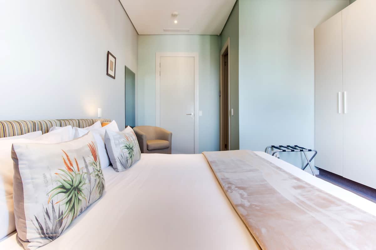 Um quarto com cama, almofadas, uma cadeira e um guarda-roupa.