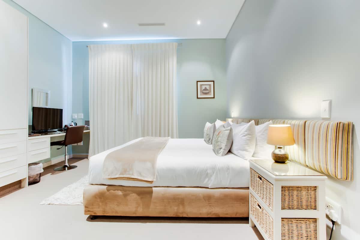 Quarto com cama, mesa de cabeceira, luminária e escrivaninha com cadeira.