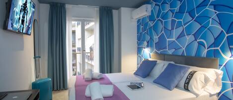 Quarto de hotel com cama, televisão, mala e vista para o exterior.