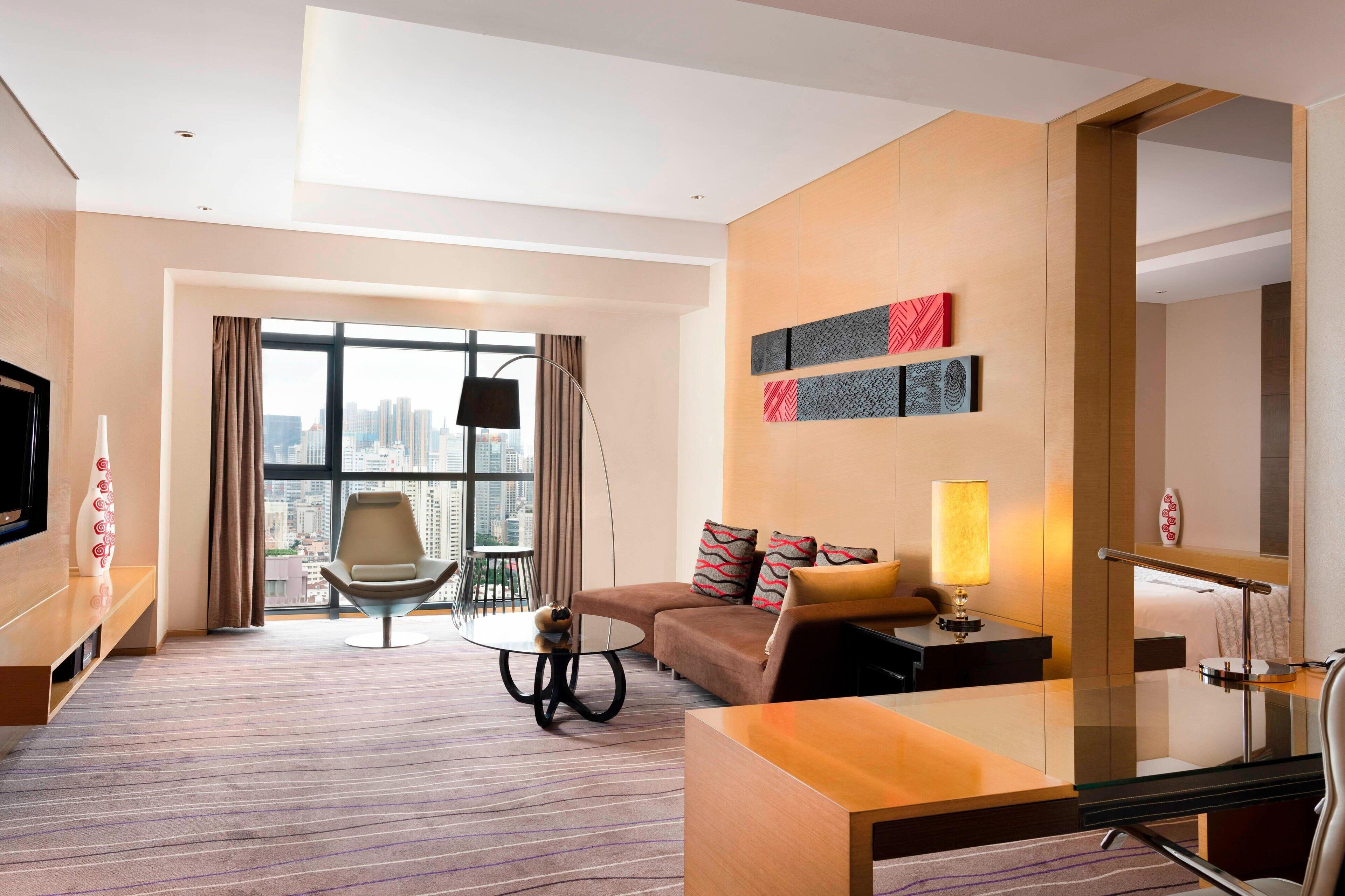 Quarto de hotel moderno com sofá, mesa pequena, abajur e televisão.