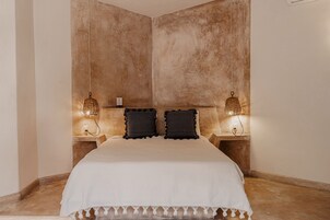 Quarto com uma cama grande, duas mesas de cabeceira e luminárias fixadas na parede.