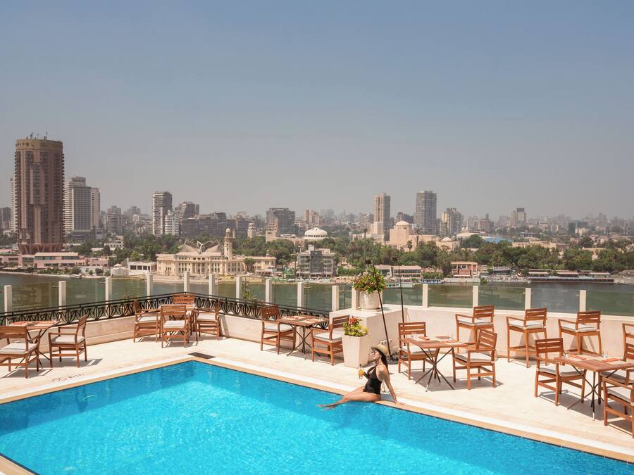 Piscina no terraço com vista para a cidade, rodeada por espreguiçadeiras e mesas.