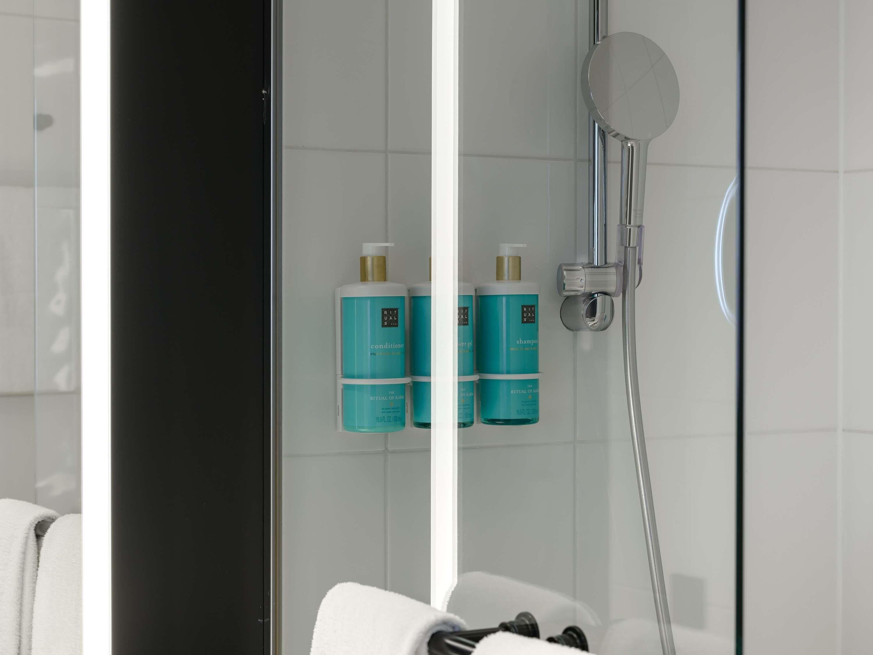 Um banheiro moderno com box de vidro, uma toalha branca e dois frascos de shampoo e condicionador Ritual of Kind.