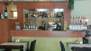 Interior de restaurante com área de bar, mesas e cadeiras de madeira.