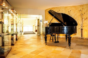 Um piano de cauda em um hall amplo, com piso xadrez e vitrines de vidro.
