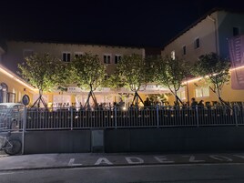 Um edifício com mesas ao ar livre sob guarda-sóis, uma bicicleta estacionada em frente e uma cerca com a palavra 'LADEZZA' escrita.