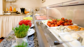 Buffet com diversos alimentos, incluindo legumes fatiados, tomates cereja e doces.