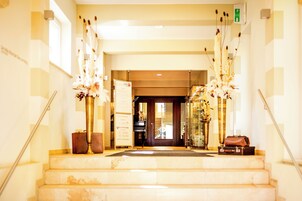 Um saguão de hotel com escadas de mármore, um balcão de recepção e arranjos florais decorativos.