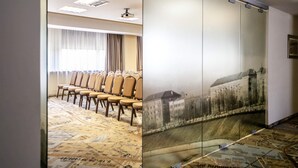 Uma sala de conferências com fileiras de cadeiras, uma janela grande com cortinas e um mapa de uma cidade no chão.