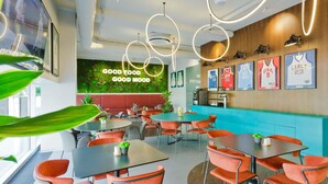 Interior de restaurante com mesas e cadeiras, uma parede com o letreiro 'GOOD FOOD GOOD MOOD' e camisas de time na parede.