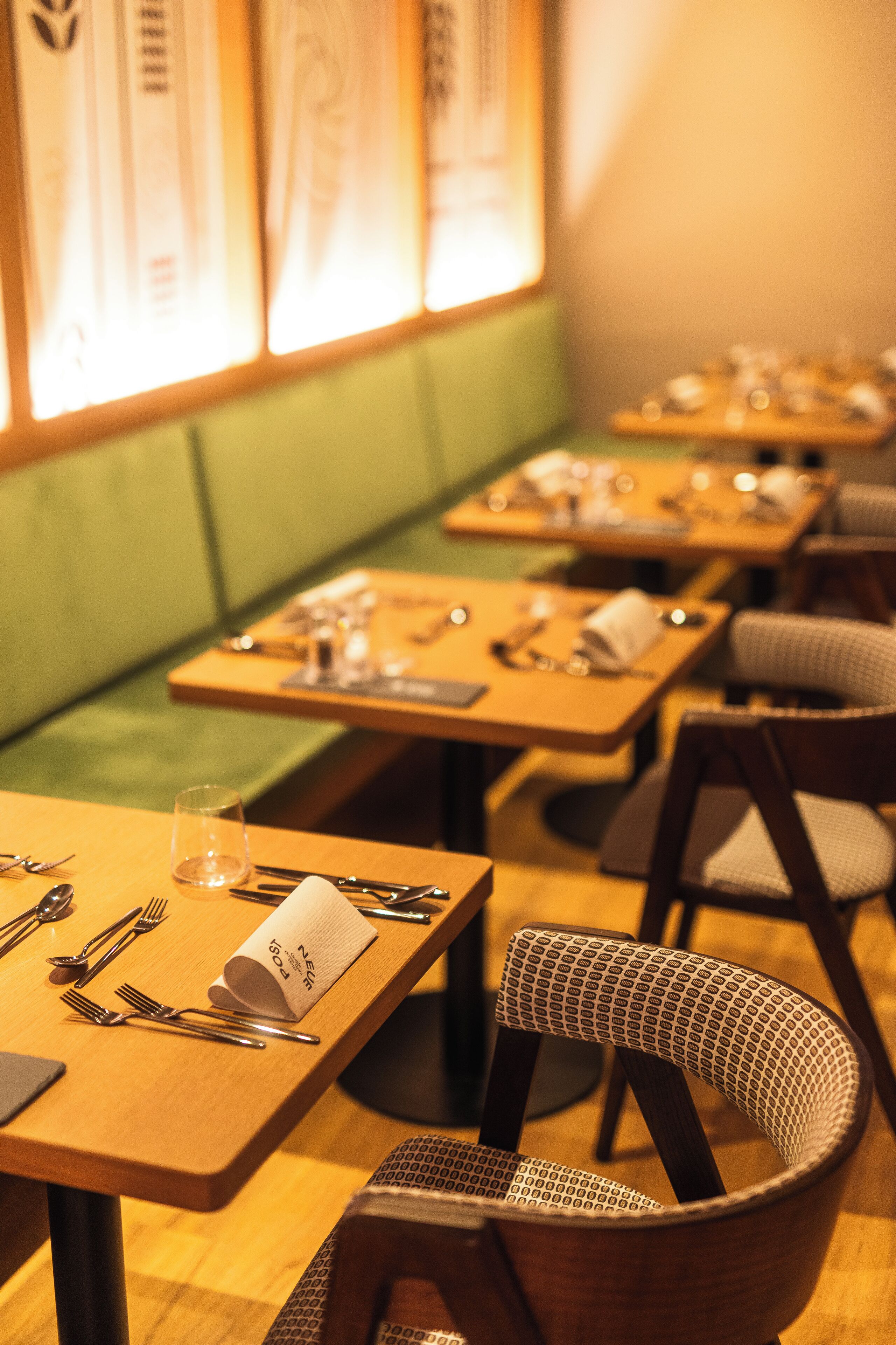Interior de restaurante com mesas de madeira, bancos acolchoados verdes e cadeiras estampadas.