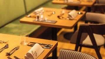 Interior de restaurante com mesas de madeira, bancos acolchoados verdes e cadeiras estampadas.