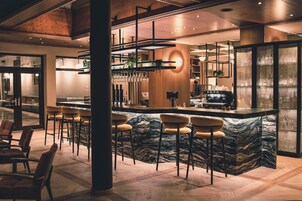 Uma área de bar moderna com bancada de mármore, banquetas e um espelho grande.