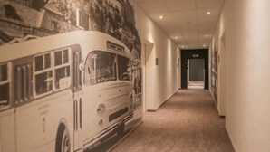 Um corredor com um grande mural de um ônibus antigo, piso coberto de carpete e uma porta no final.