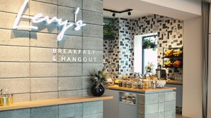 Espaço de café da manhã e convívio com design moderno, com balcão e diversas opções de comida, e uma placa de neon.