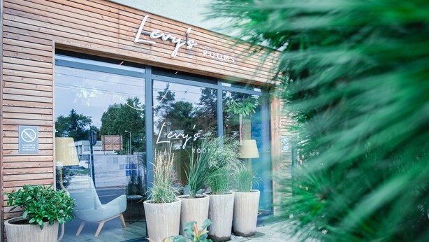 Um edifício com uma placa que diz "Leroy's Rooms" e uma porta de vidro. Há plantas em vasos na frente da entrada.
