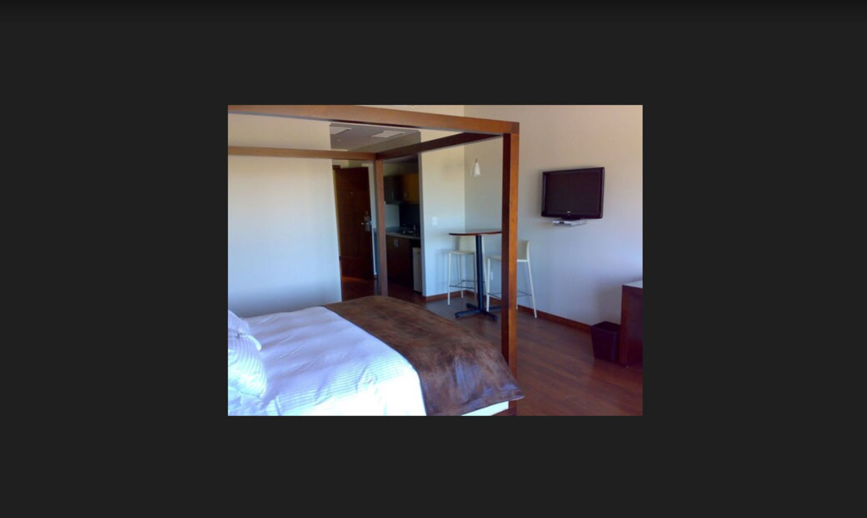 Quarto com cama, televisão e uma kitchenette ao fundo.