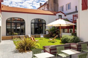 Um pátio com área de refeições, mesas ao ar livre e vista para a fachada do edifício.